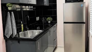Uma cozinha com armários pretos, geladeira de aço inoxidável, micro-ondas e pia.