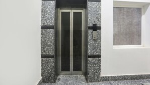 Um elevador com porta de vidro, ladeado por paredes com padrão salpicado.