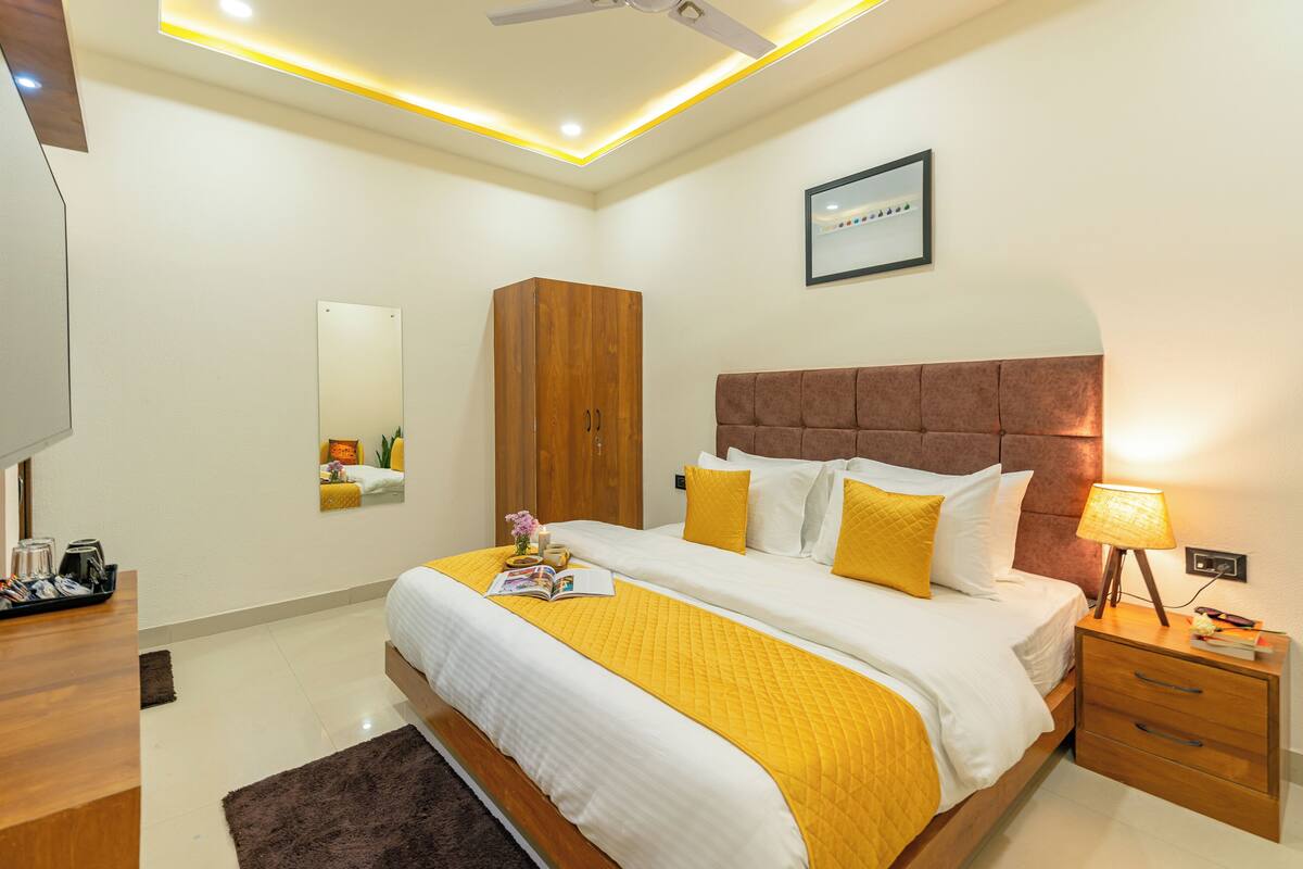 Quarto de hotel moderno com uma cama grande, guarda-roupa de madeira, mesa de cabeceira e ventoinha no teto.
