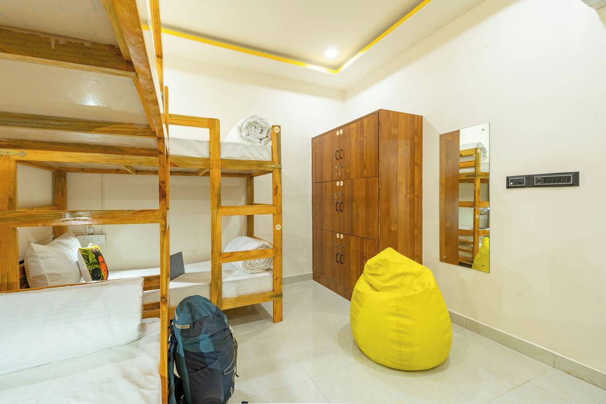 Quarto tipo dormitório com beliches, guarda-roupa de madeira, um bean bag amarelo e um espelho na parede.