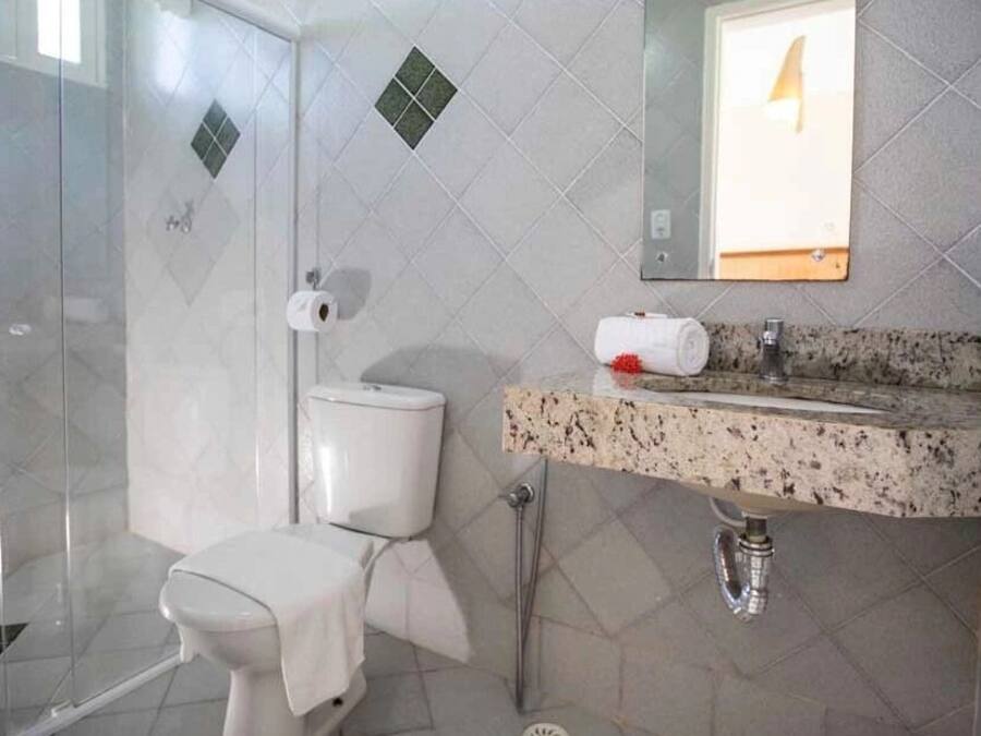 Casa de banho com cabine de chuveiro em vidro, sanita branca e lavatório com bancada em granito.