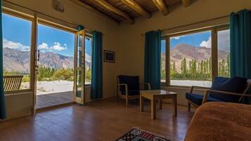 Quarto com teto de madeira, uma cama, um sofá, uma mesa e cadeiras. Janelas amplas com vista para as montanhas.