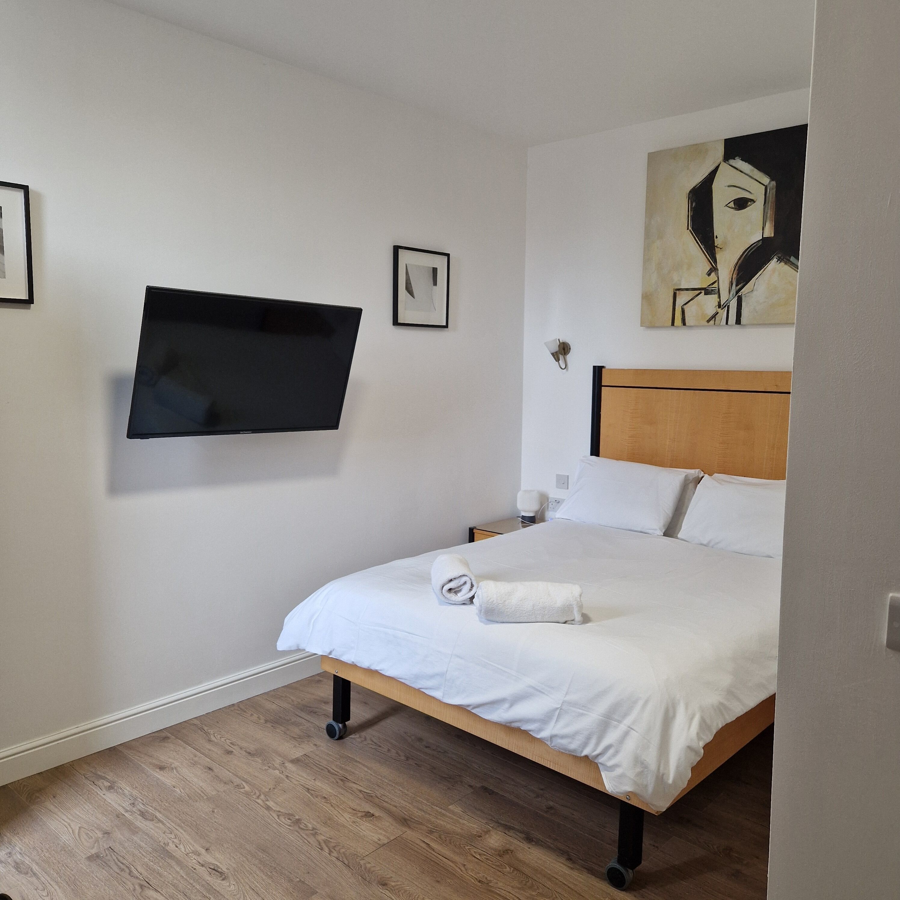 Quarto com uma cama, televisão de tela plana na parede e um quadro sobre a cama.