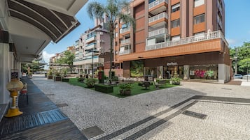 Um edifício moderno com várias varandas, um pátio central com plantas e uma loja com uma placa visível.