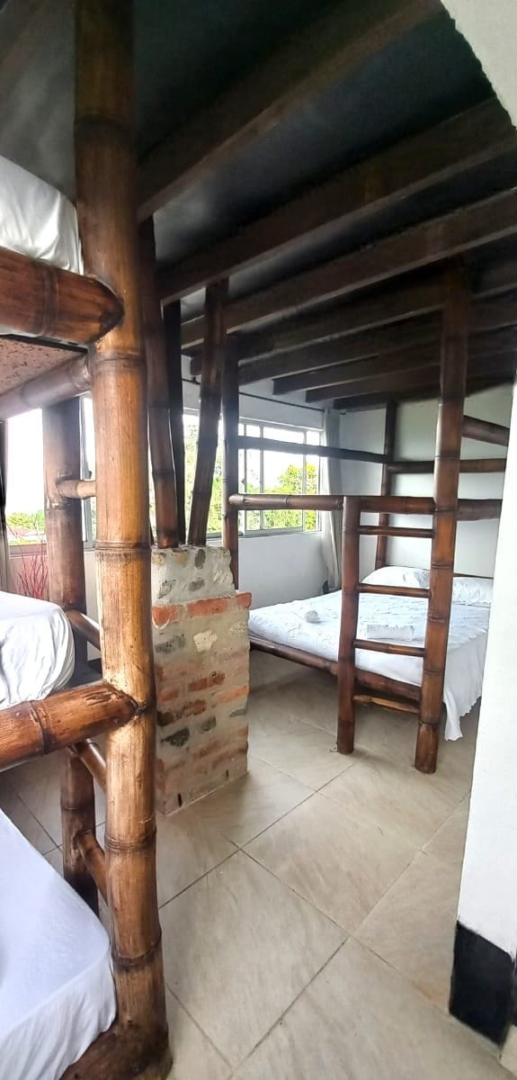 Um quarto rústico com pilares de bambu, parede de tijolos e cama com roupa de cama branca.