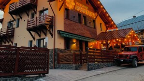 Uma pousada de montanha tradicional com varandas de madeira, uma placa com a inscrição "MONTANA" e um veículo vermelho estacionado na frente.