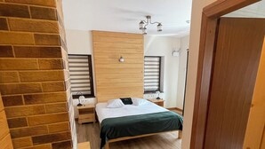Quarto moderno com cabeceira de madeira, cama com colcha verde, mesa de cabeceira, abajur e janela com persianas.