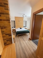 Quarto moderno com cabeceira de madeira, cama com colcha verde, mesa de cabeceira, abajur e janela com persianas.