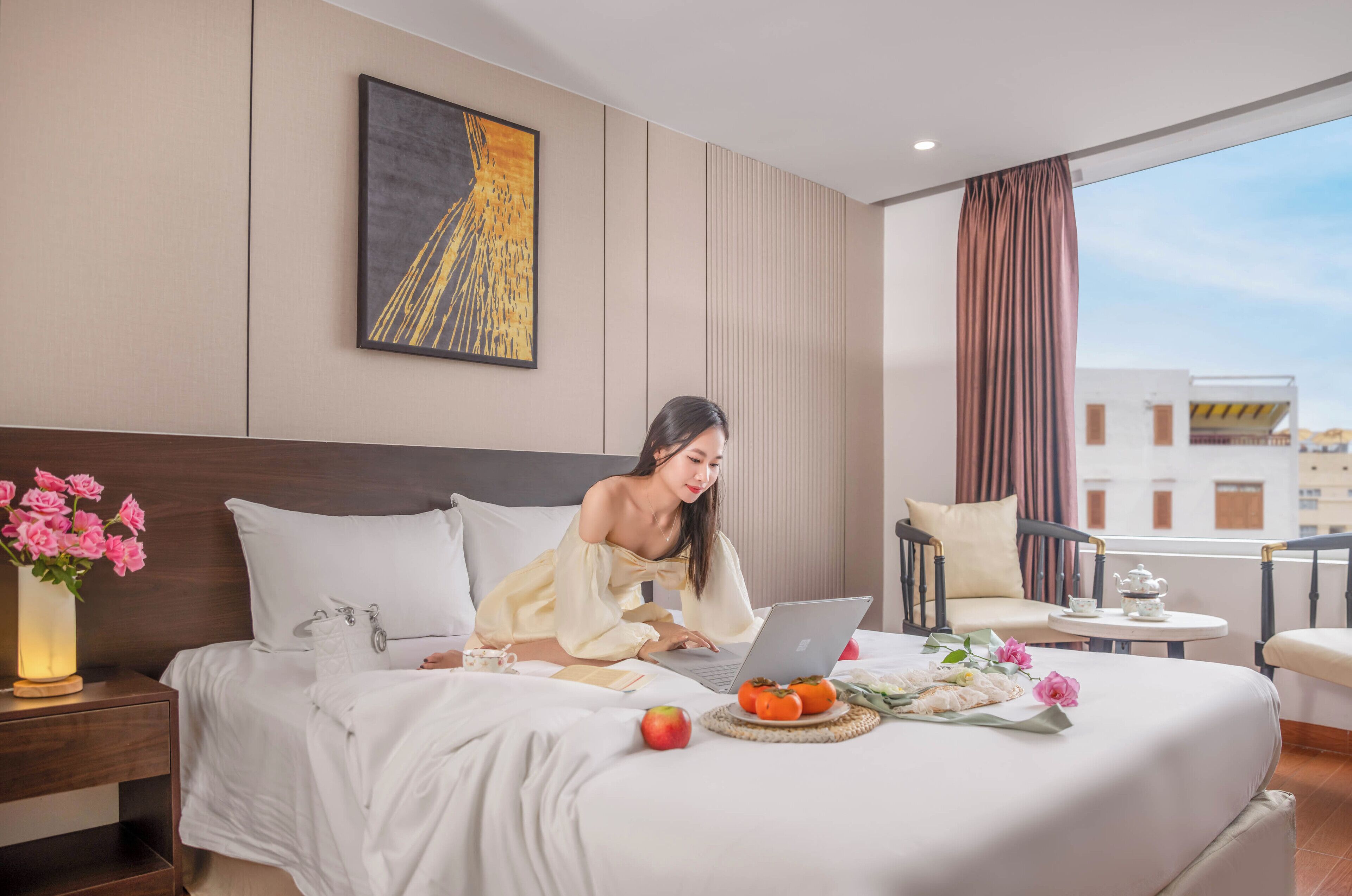 Quarto de hotel com cama, laptop, vaso de flores e mesa com bule.