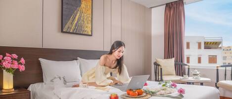 Quarto de hotel com cama, laptop, vaso de flores e mesa com bule.