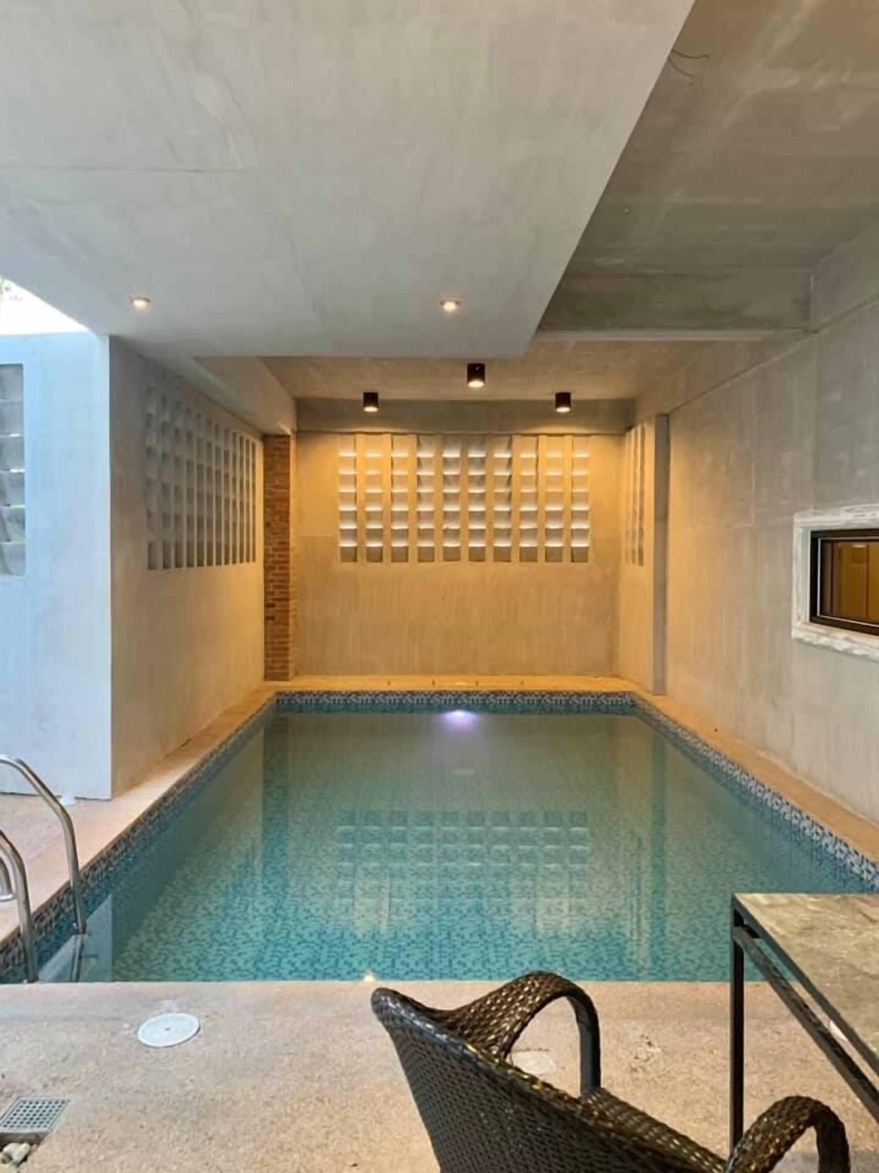 Uma piscina com borda azulejada, uma cadeira e uma mesa pequena.