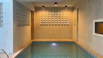 Uma piscina com borda azulejada, uma cadeira e uma mesa pequena.
