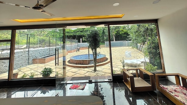Quarto amplo com grande janela que oferece vista para um pátio com fonte, área de estar e vegetação.