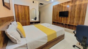 Quarto de hotel com cama, escrivaninha, cadeira, televisão e ventoinha no teto.
