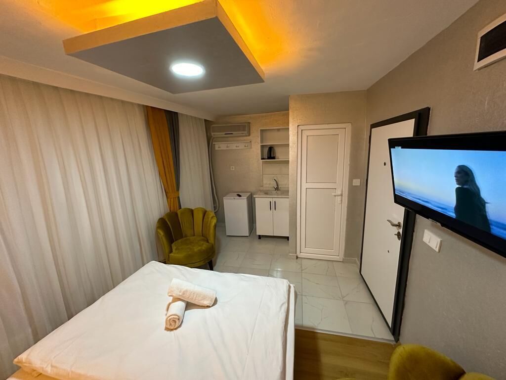 Quarto de hotel com cama, televisão, pequena cozinha e porta que dá para outro aposento.