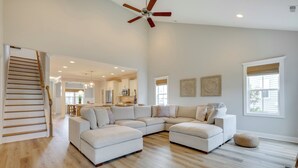 Uma sala de estar espaçosa com um amplo sofá modular, uma escada de madeira e um ventilador de teto.
