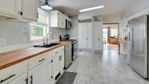 Cozinha moderna com armários brancos, eletrodomésticos de aço inoxidável e bancada de madeira.