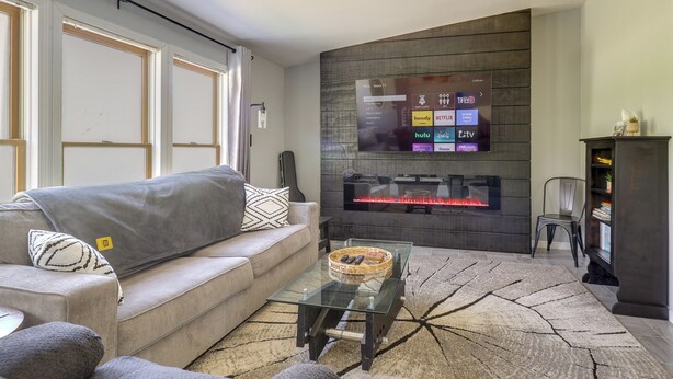 Uma sala de estar moderna com sofá, mesa de centro de vidro, lareira e televisão de tela plana na parede.