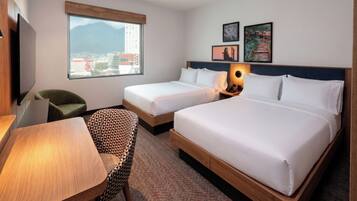 Quarto de hotel com duas camas, uma escrivaninha, uma cadeira e uma televisão.