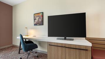 Quarto moderno com escrivaninha branca, cadeira de escritório azul, televisão de tela plana, armário de madeira e uma cadeira vermelha.