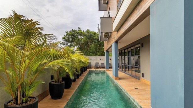 Uma piscina interior estreita, com plantas em vasos de um lado e um edifício com grandes janelas do outro.