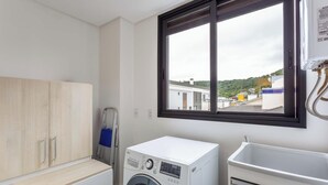 Uma lavanderia com máquina de lavar, pia e janela com vista para edifícios.
