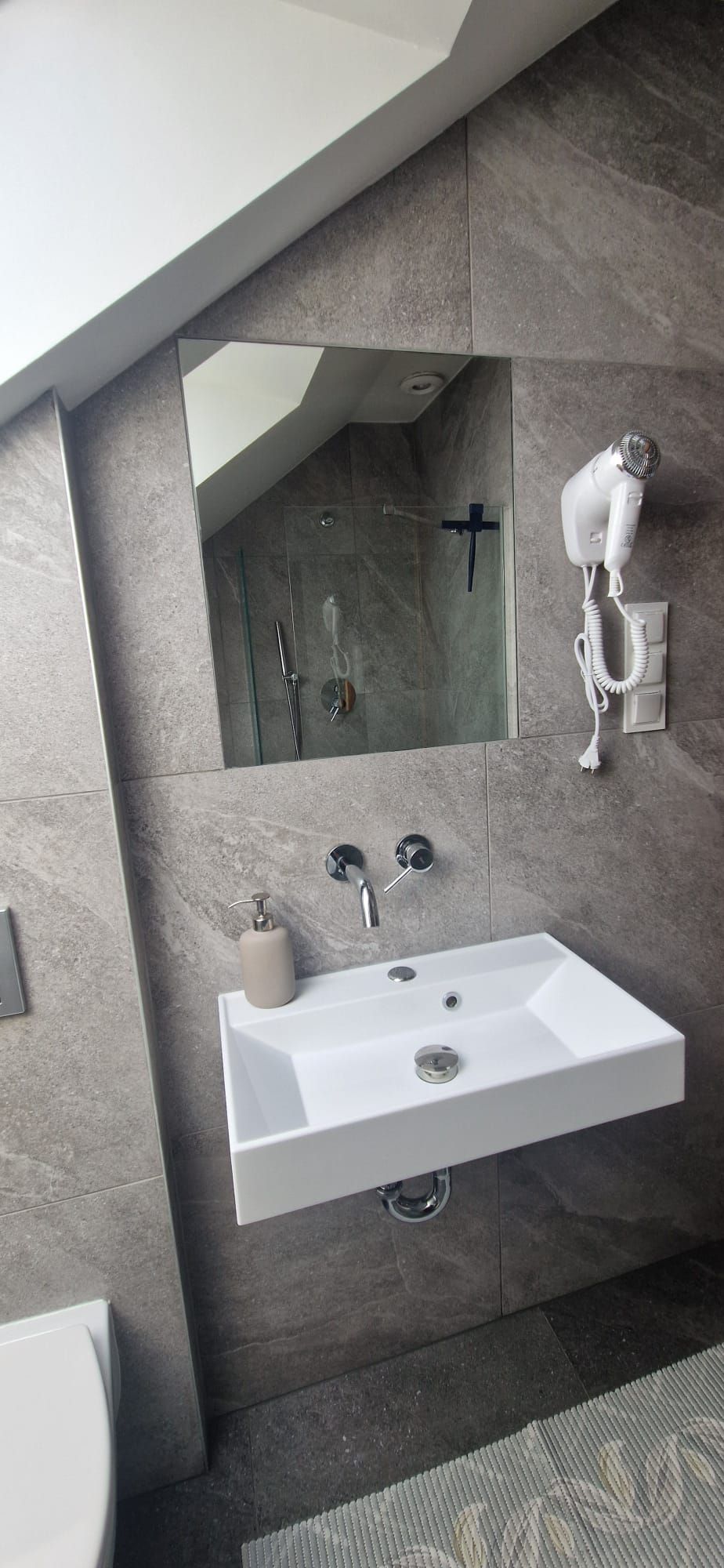 Uma casa de banho moderna com lavatório embutido, secador de cabelo fixado na parede e cabine de duche em vidro.
