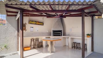 Uma área de cozinha externa com mesa de pedra, banquetes e uma placa pendurada.