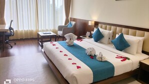 Quarto de hotel com uma cama grande, uma escrivaninha, uma cadeira e janela com cortinas.