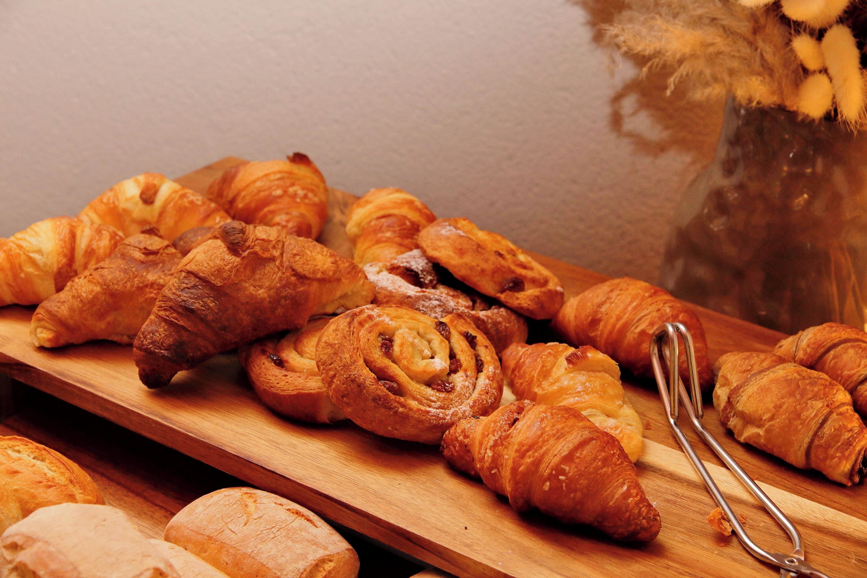 Diversos pastéis em uma tábua de madeira, incluindo croissants e pão.