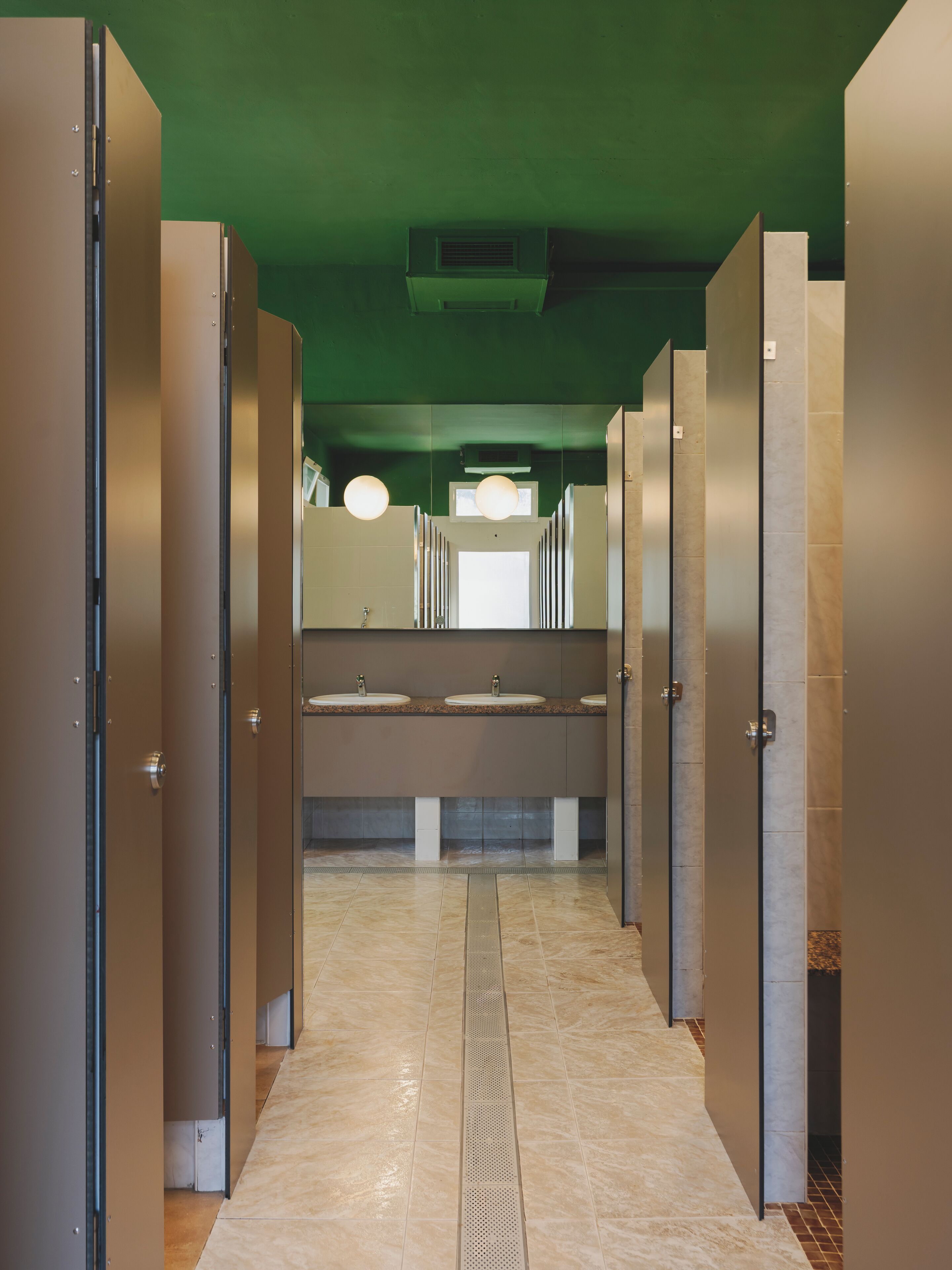 Corredor com vários boxes de banheiro, cada um com espelho e pia.