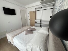 Quarto de hotel com cama, televisão de tela plana na parede, porta e janela com cortinas.