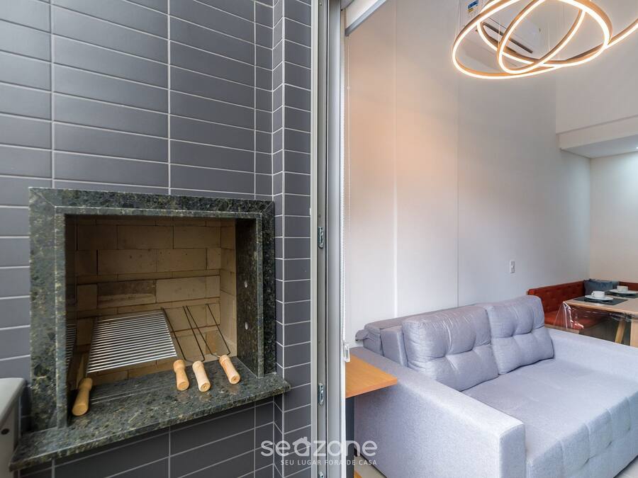 Interior moderno com parede revestida de azulejos cinzas, lareira com grade de metal e sofá cinza num canto.
