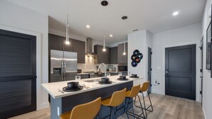 Cozinha moderna com ilha central, banquetas, eletrodomésticos de aço inoxidável e luminárias pendentes.