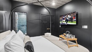 Quarto de hotel moderno com uma cama, uma TV fixada na parede e um suporte com chaleira e bule.