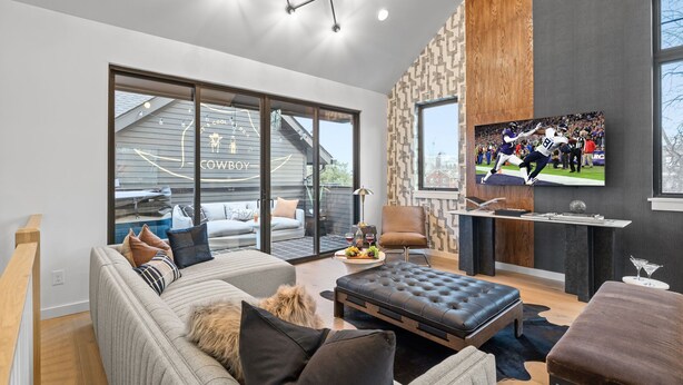 Uma sala de estar moderna com uma televisão grande, assentos confortáveis e vista para uma casa chamada 'COWBOY'.