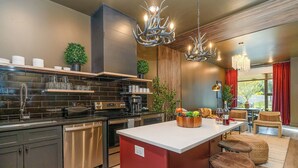Uma cozinha moderna com eletrodomésticos de aço inoxidável, uma ilha central e uma área de jantar com cortinas vermelhas e um candelabro.