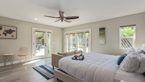 Quarto com cama, ventilador de teto, janela e porta que dá para área externa.