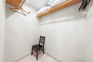 Quarto pequeno e pouco mobiliado, com uma cama de madeira em beliche, uma cadeira e uma parede branca.