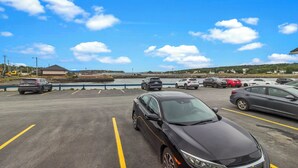 Um parque de estacionamento com vários carros, céu claro e edifícios ao longe.