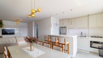 Uma cozinha moderna com armários brancos, uma ilha central e um espaço de refeições com mesa e cadeiras brancas.