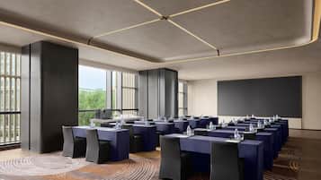 Sala de conferência com várias mesas, cadeiras e um ecrã grande.