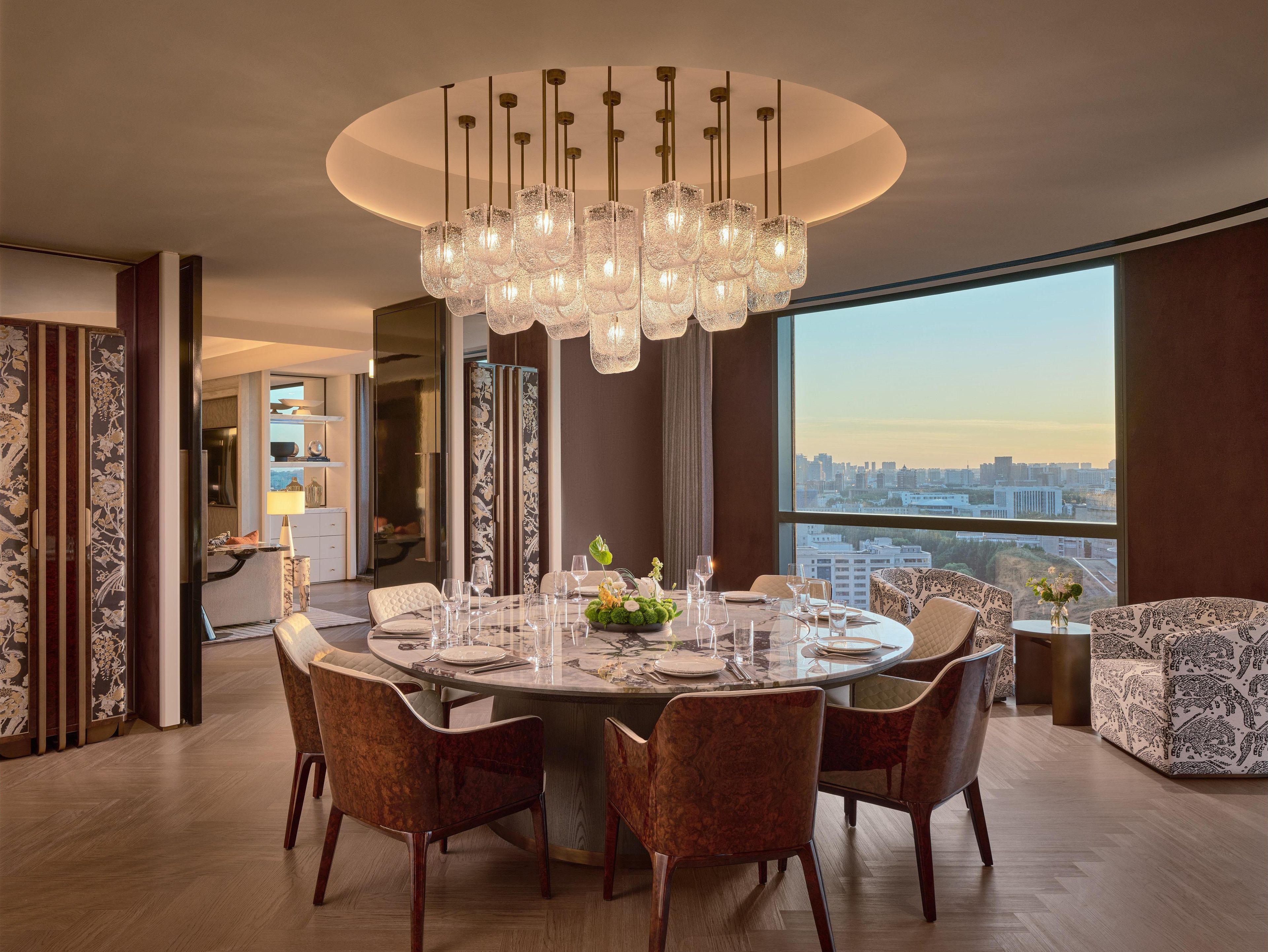 Uma sala de jantar moderna com uma mesa redonda, várias cadeiras e um candelabro.