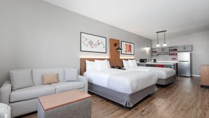 Quarto de hotel moderno com sofá, duas camas, pequena cozinha e obras de arte nas paredes.