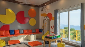 Uma área de recreação infantil moderna, com mobiliário colorido, mesa de pebolim e uma grande janela com vista.