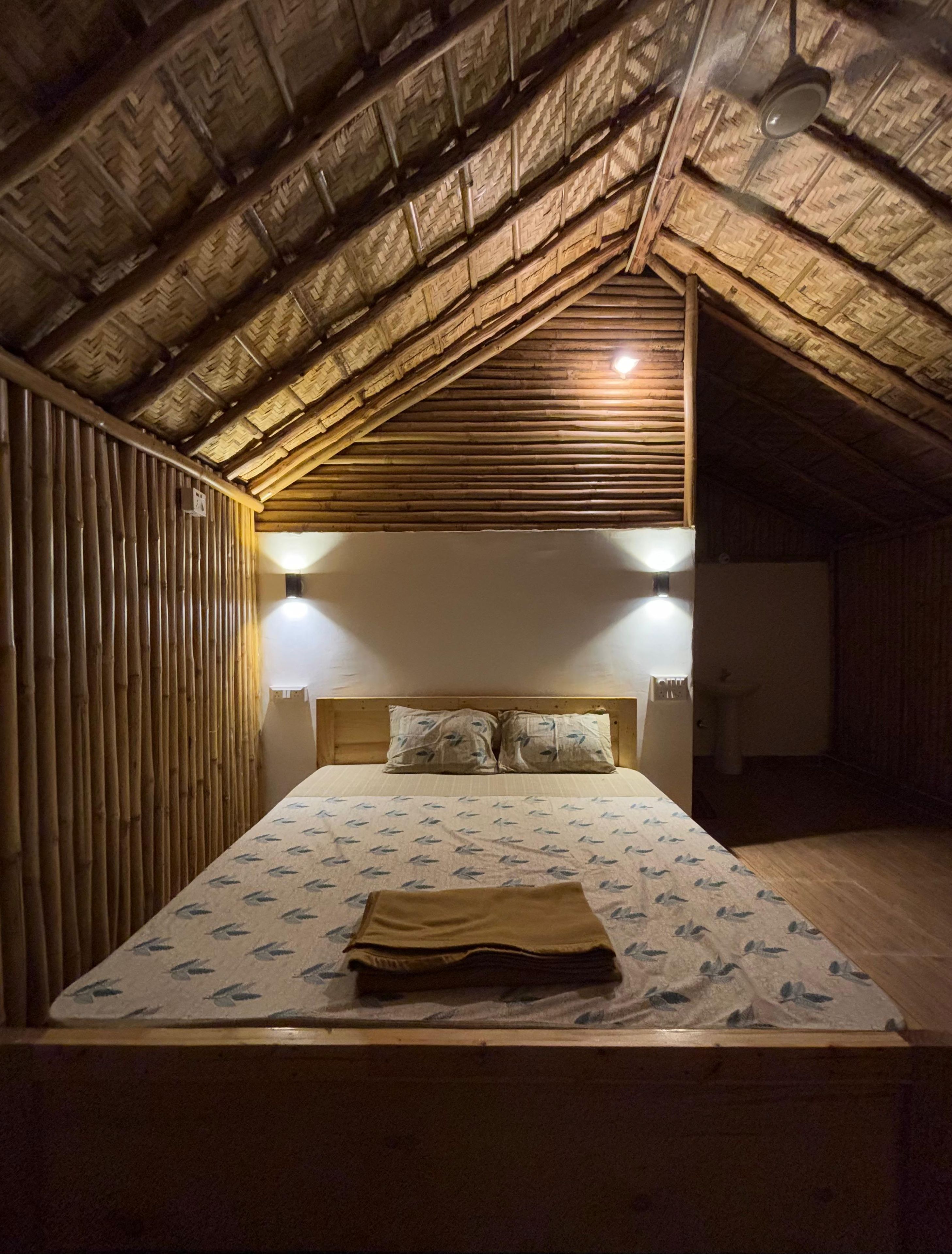 Quarto com teto inclinado, cama com colcha estampada, duas luzes fixadas na parede e cabeceira de madeira.