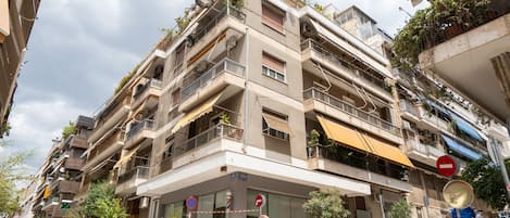 Um edifício com várias andares, sacadas, placa de proibido estacionar e carros estacionados.