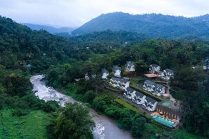 Um resort numa encosta com vários edifícios brancos, uma piscina e um rio a correr pelo terreno.