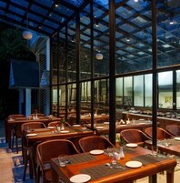 Restaurante com teto de vidro moderno, mesas e cadeiras de madeira.