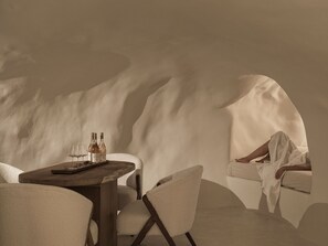 Um interior acolhedor com uma mesa posta para dois, uma cadeira e uma pessoa relaxando num sofá.